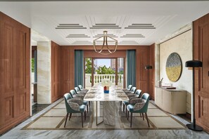 Uma sala de jantar espaçosa com uma mesa comprida posta para refeição, ladeada por painéis de madeira e vista para o exterior.