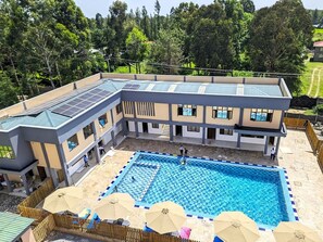 Um edifício de vários andares com piscina, painéis solares no telhado e área externa cercada.