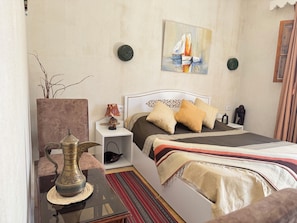 Quarto com cama, mesas de cabeceira, abajur, um vaso decorativo, um quadro e tapete.