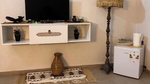Sala de estar com televisão de tela plana, luminária, cafeteira, vaso e uma geladeira compacta.