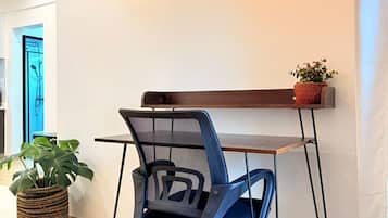 Uma cadeira de escritório moderna com encosto em tela e rodízios, colocada em uma escrivaninha com tampo de madeira e pés de metal preto.