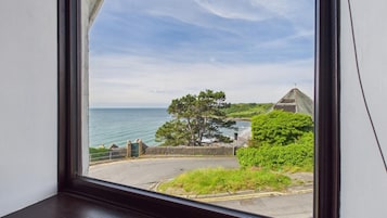 Vista costeira através de uma janela, incluindo uma estrada, uma árvore e um edifício com telhado cónico.
