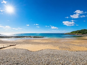 Uma praia com pedras, uma costa rochosa e um céu azul límpido.