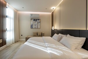 Quarto de hotel moderno com uma cama grande, uma mesa de cabeceira, um sofá e um aparelho de ar condicionado.