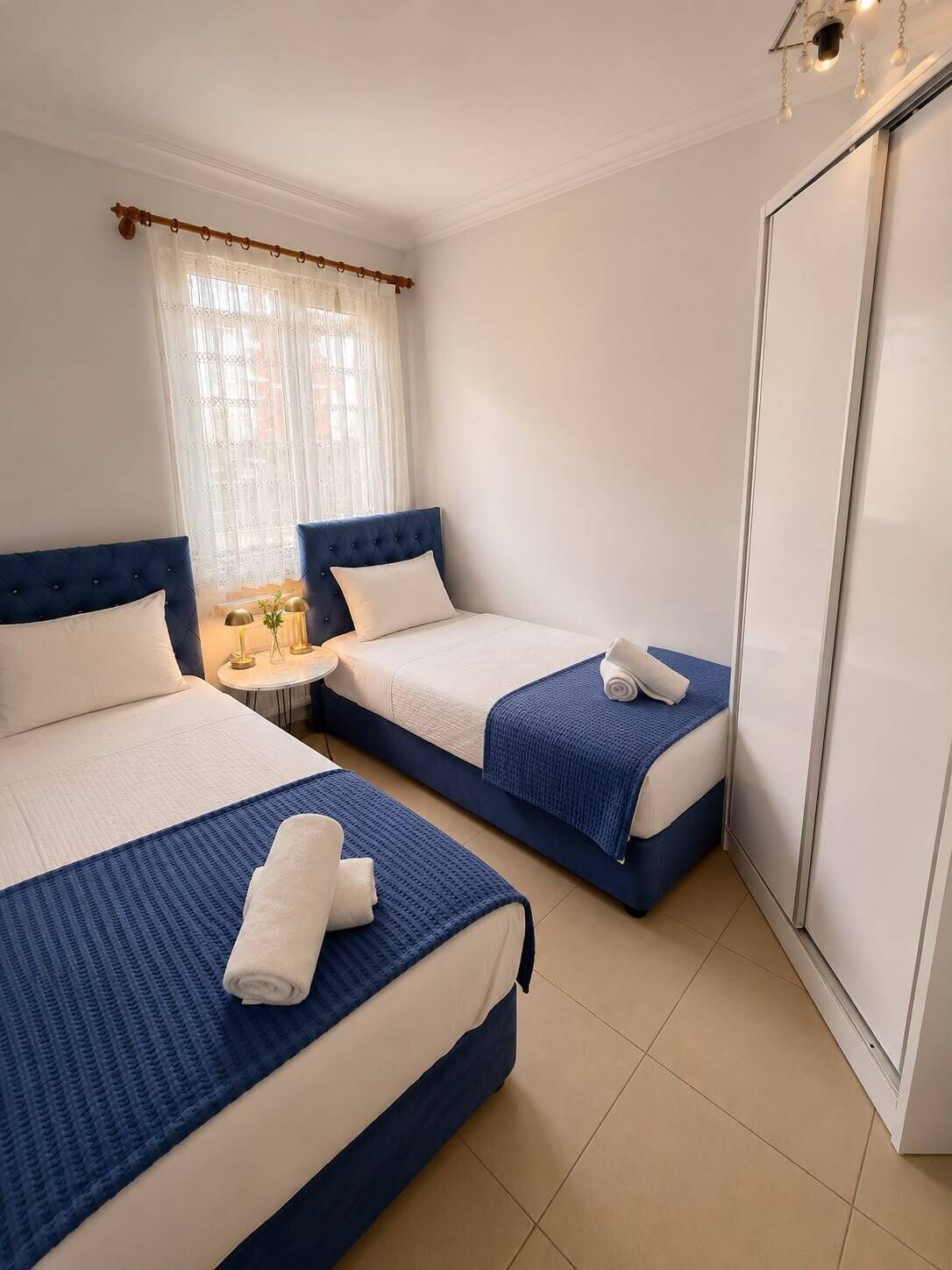 Quarto de hotel com duas camas, uma mesinha e um guarda-roupa.