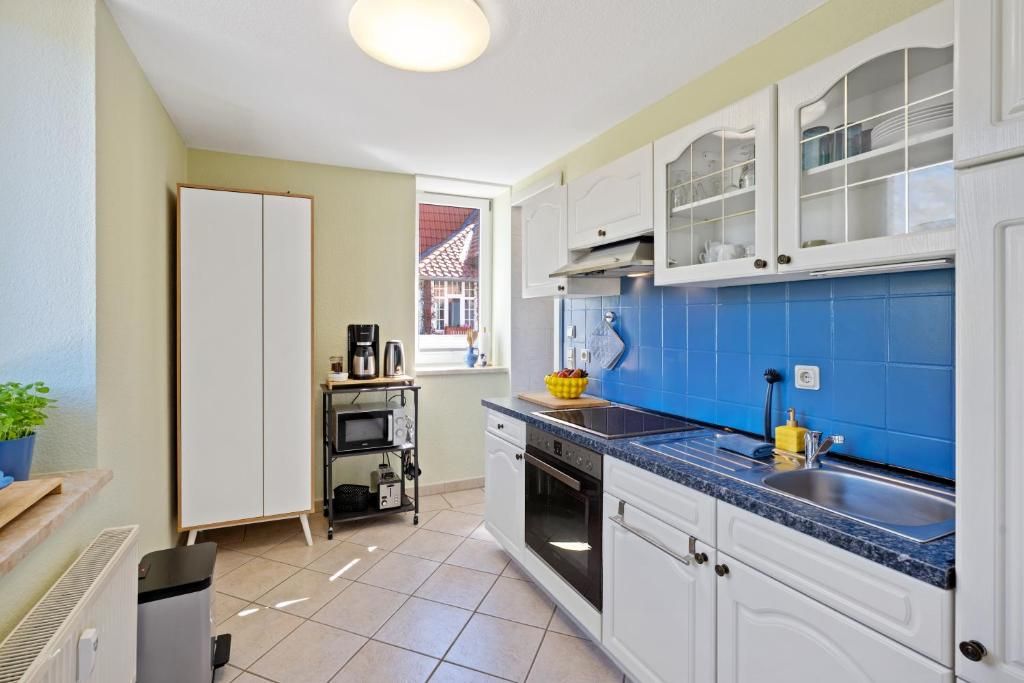 Cozinha compacta com armários brancos, painel de azulejos azuis e uma janela com vista para um edifício.