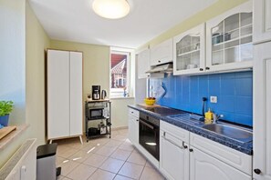 Cozinha compacta com armários brancos, painel de azulejos azuis e uma janela com vista para um edifício.