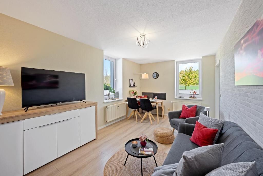 Uma sala de estar moderna com televisão de tela plana, sofá cinzento e um espaço de jantar com mesa e cadeiras.