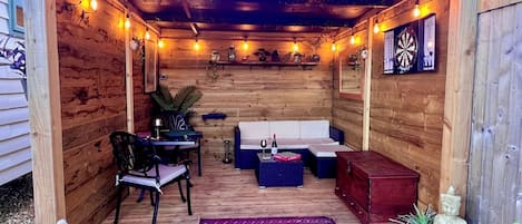 Quarto de madeira com um sofá, cadeiras, uma mesa e um alvo de dardos.