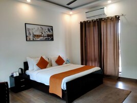 Quarto com cama, mesa de cabeceira, ar condicionado fixado na parede e janela com cortinas.