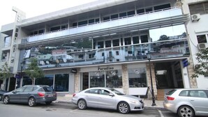 Um edifício moderno com fachada de vidro, uma loja chamada 'Paradiso' e carros estacionados na rua.