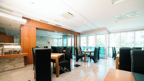 Um restaurante moderno com parede de pedra, mesas de madeira e cadeiras pretas.