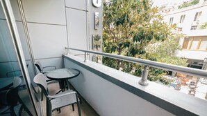 Uma varanda com mesa e cadeiras, um corrimão e vista para edifícios e árvores.