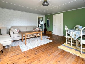 Sala de estar com sofá, mesa de centro, mesa de jantar e cadeiras, e uma porta.