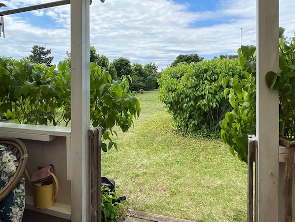 Visão através de uma porta para um jardim com um caminho gramado, rodeado por vegetação exuberante.