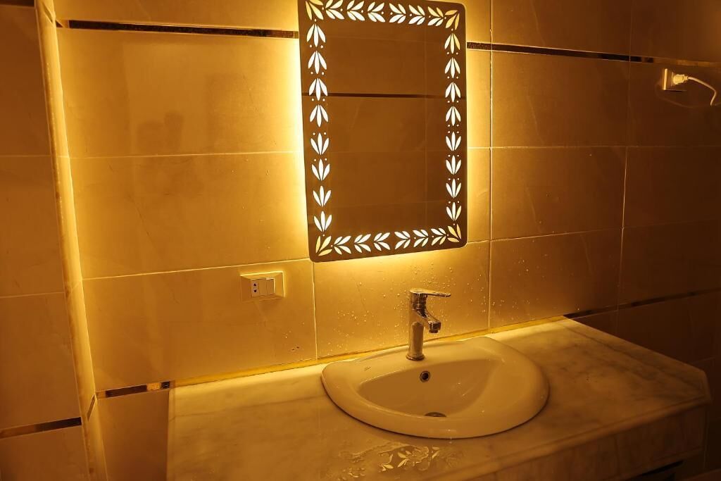 Casa de banho com lavatório, espelho e candeeiro na parede.