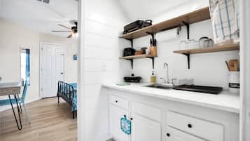 Uma cozinha moderna com armários brancos, prateleiras de madeira, uma pia e um ventilador de teto.