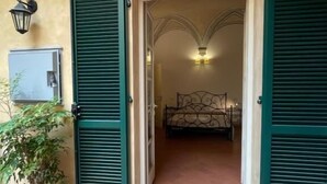 Uma porta com portões verdes abertos que dá para um quarto com cama e luminária na parede.