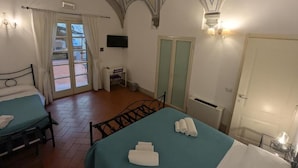 Quarto de hotel com duas camas, uma mesa de jantar, uma cadeira, uma televisão e uma porta.