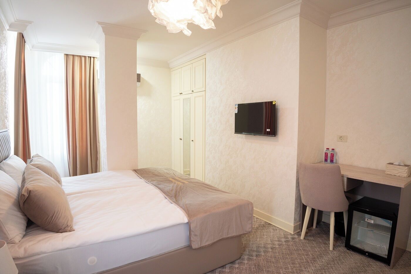 Quarto de hotel com uma cama, escrivaninha, televisão e minibar.