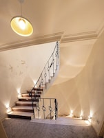 Escada em espiral com corrimão preto, degraus carpetados e luminária pendente.