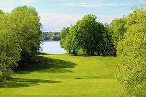 Um campo de golfe com um lago ao fundo, rodeado por árvores.