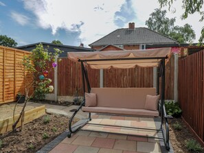 Um jardim com baloiço, cerca de madeira e uma casa ao fundo.