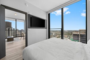 Quarto de hotel moderno com uma cama grande, televisão de tela plana na parede e varanda com vista para a cidade.