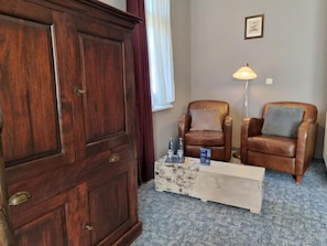 Quarto com guarda-roupa de madeira, duas poltronas de couro, uma mesa de centro e um abajur.