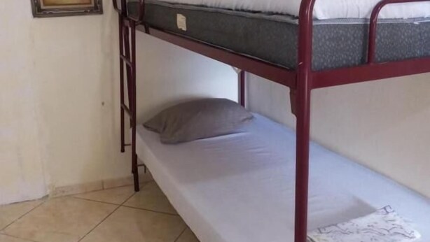 Uma cama beliche com colchão e travesseiros, um quadro na parede e um chão revestido de azulejos.