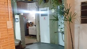 Um corredor com chão de azulejos, um vaso de plantas, uma porta com alarme de incêndio e uma parede de tijolos.