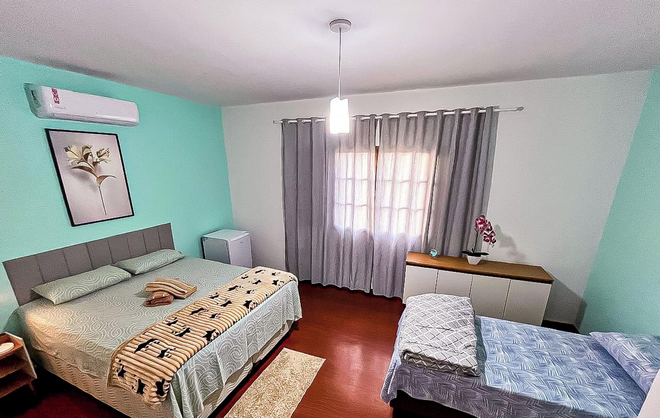 Quarto com cama, escrivaninha, cadeira e janela com cortinas.
