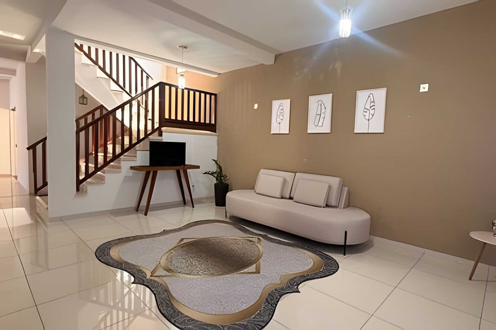 Uma sala de estar com escada, sofá, mesa de centro e obras de arte nas paredes.