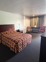 Quarto de hotel com uma cama grande, uma escrivaninha, uma cadeira e uma mesinha.