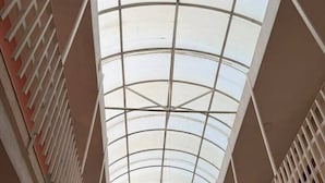 Um átrio em vários níveis com teto de vidro, varandas e um elevador central.