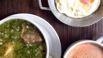 Mesa de café da manhã com uma tigela de sopa, um prato com ovo, uma xícara de café e um copo de suco de laranja.