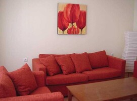 Uma sala de estar com um sofá vermelho, uma mesa de centro de madeira e um quadro de flores vermelhas na parede.