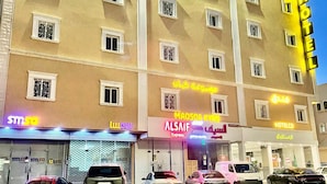 Um hotel de vários andares com fachada amarela, várias janelas e diversos estabelecimentos comerciais no térreo.