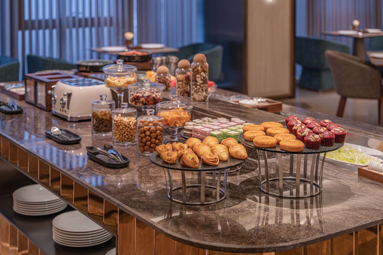 Um buffet com diversos alimentos, incluindo pastéis e sobremesas, disposto em um balcão de mármore.