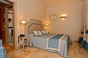 Quarto com cama, luminárias de cabeceira, mesa de cabeceira, luz acoplada na parede e porta para outro cômodo.