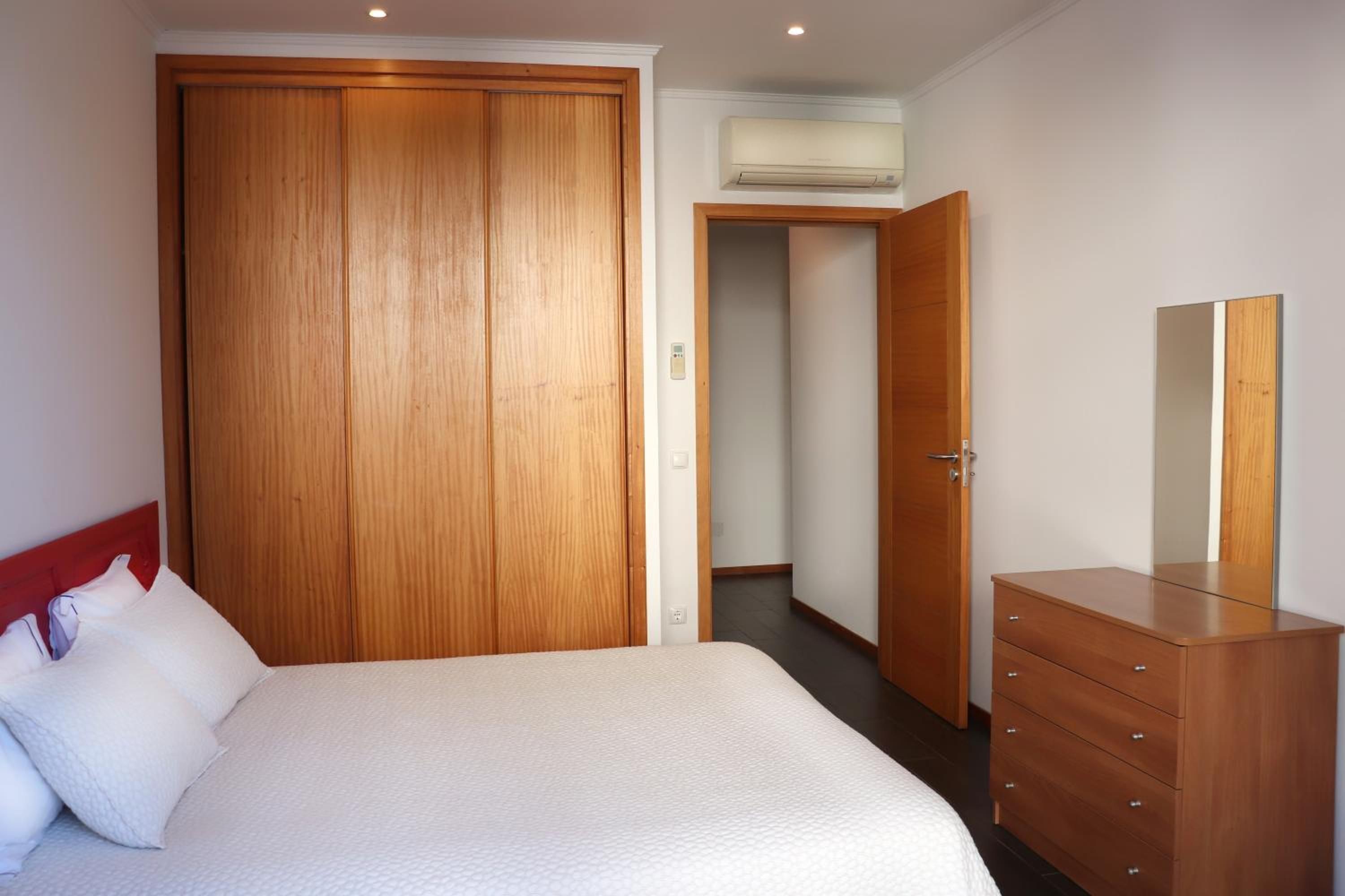 Quarto com cama, guarda-roupa de madeira e cômoda.