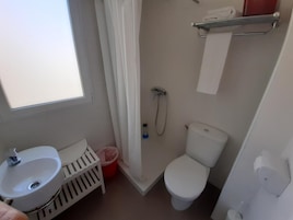 Uma casa de banho pequena com sanita, lavatório, chuveiro e janela.