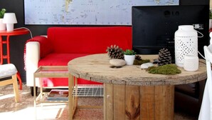 Um quarto com uma mesa de madeira redonda, sofá vermelho e um mapa-múndi na parede.