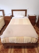 Quarto de hotel padrão com uma cama de solteiro, duas mesinhas de cabeceira de madeira e cabeceira de madeira.
