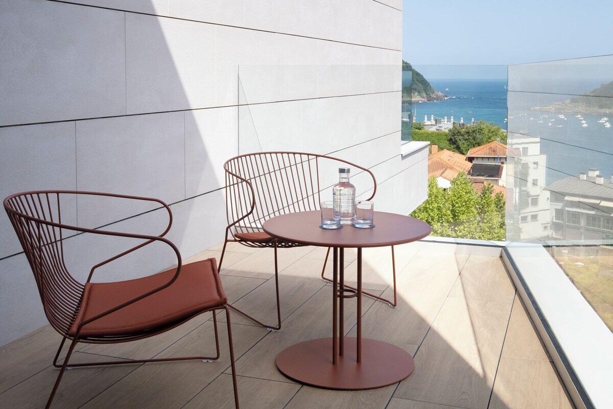 Uma varanda com mesa e duas cadeiras, com vista para o litoral.