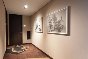 Um corredor com obras de arte nas paredes, piso coberto de carpete e uma porta no final.