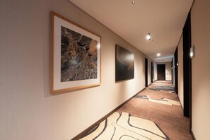 Um corredor com obras de arte emolduradas nas paredes, piso coberto por carpete e design moderno no teto.