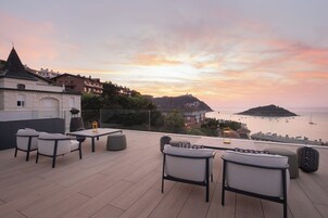 Um terraço com mesas ao ar livre e vista para o mar e uma colina com edifícios.
