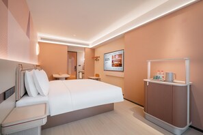 Quarto de hotel com cama, mesa de cabeceira e uma pequena mesa com uma cadeira. Há uma TV fixada na parede e um espelho sobre a mesa.