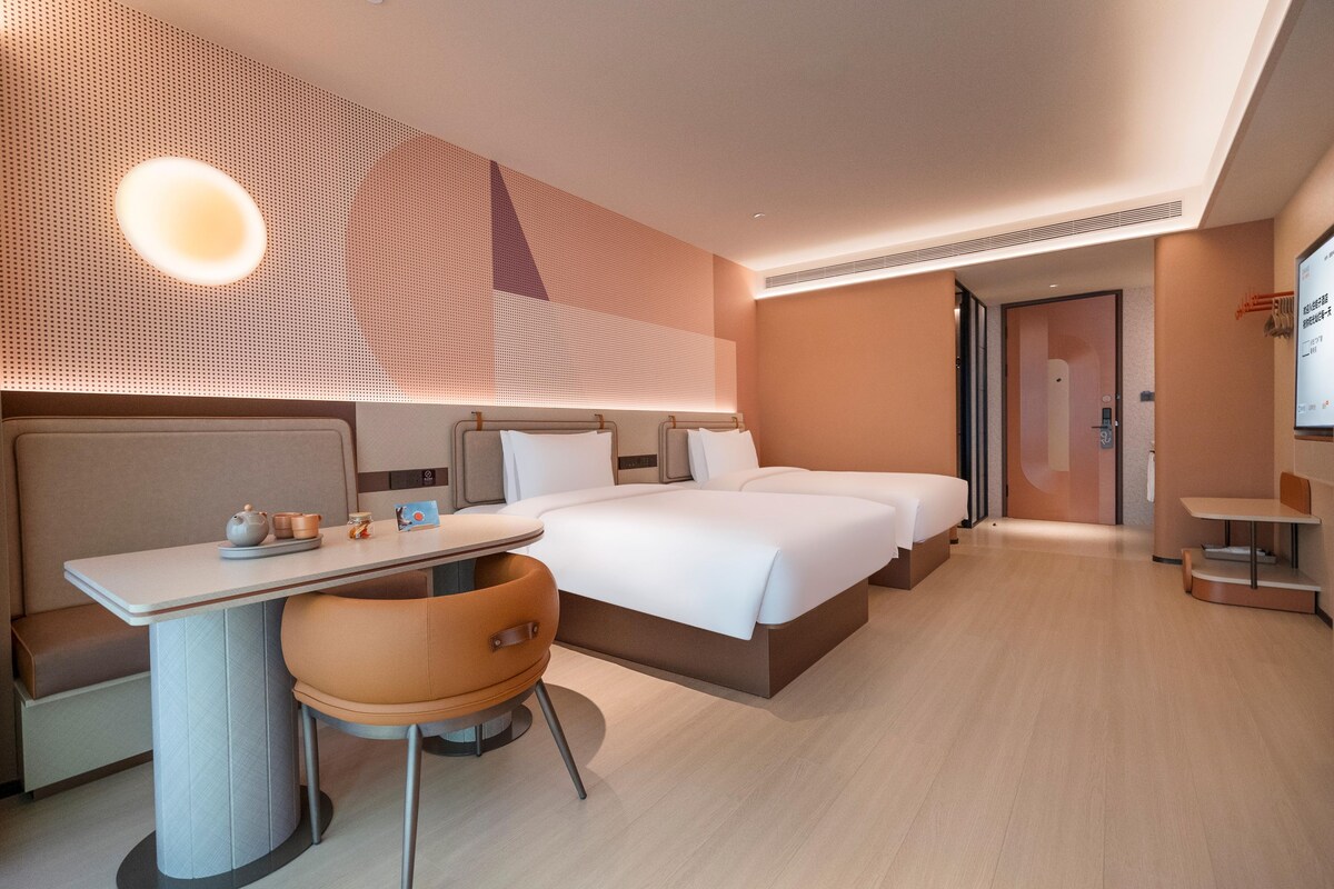 Quarto de hotel moderno com uma cama grande, uma mesa com cadeira e uma mesinha.